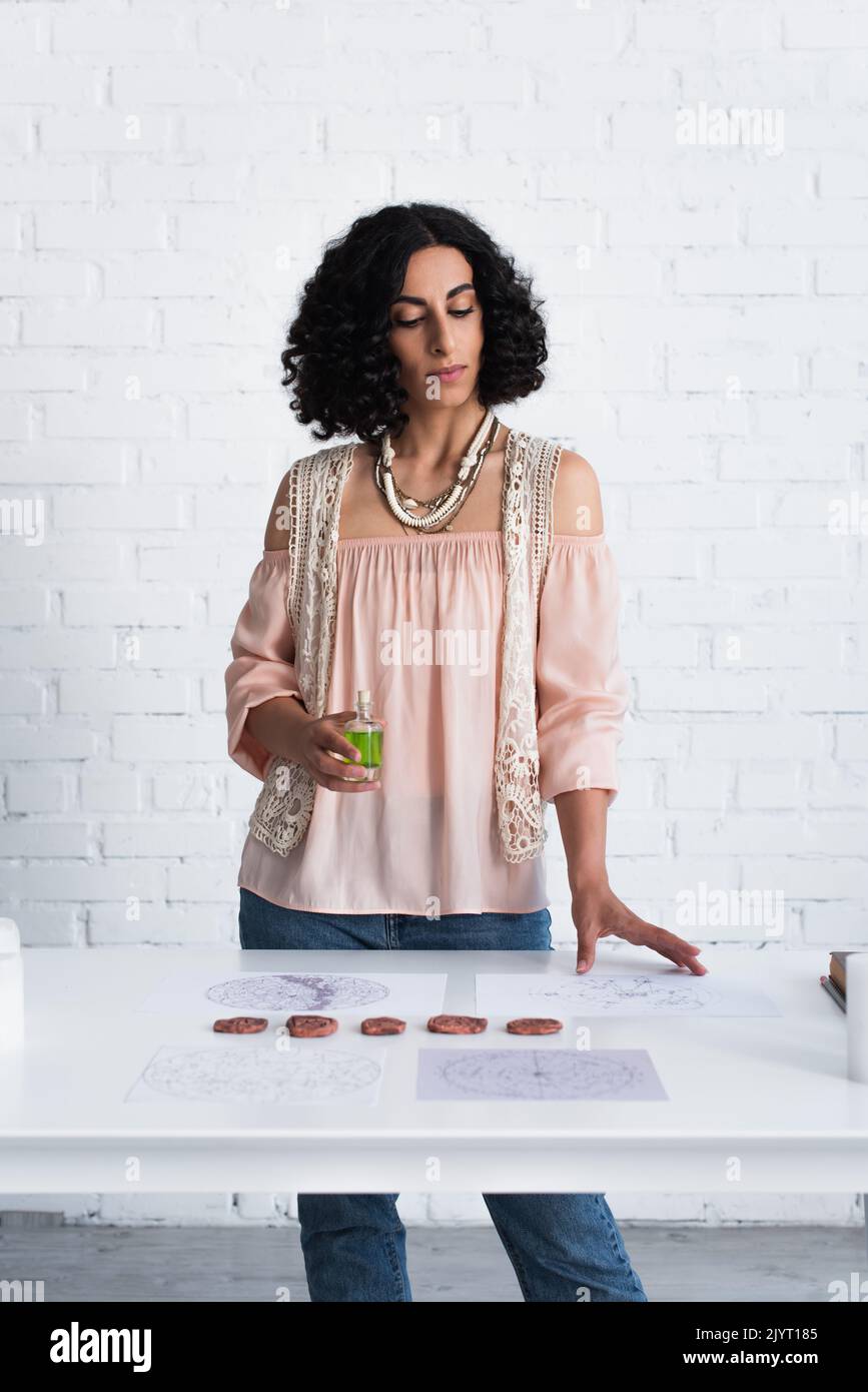 brunette astrologist with bottle of essential oil standing near clay ...