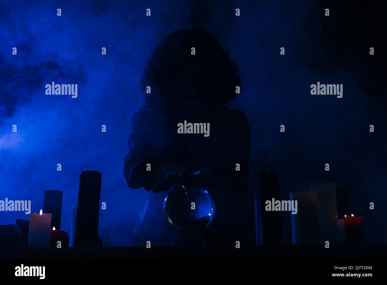 fortune teller holding hand above crystal ball near burning candles in ...