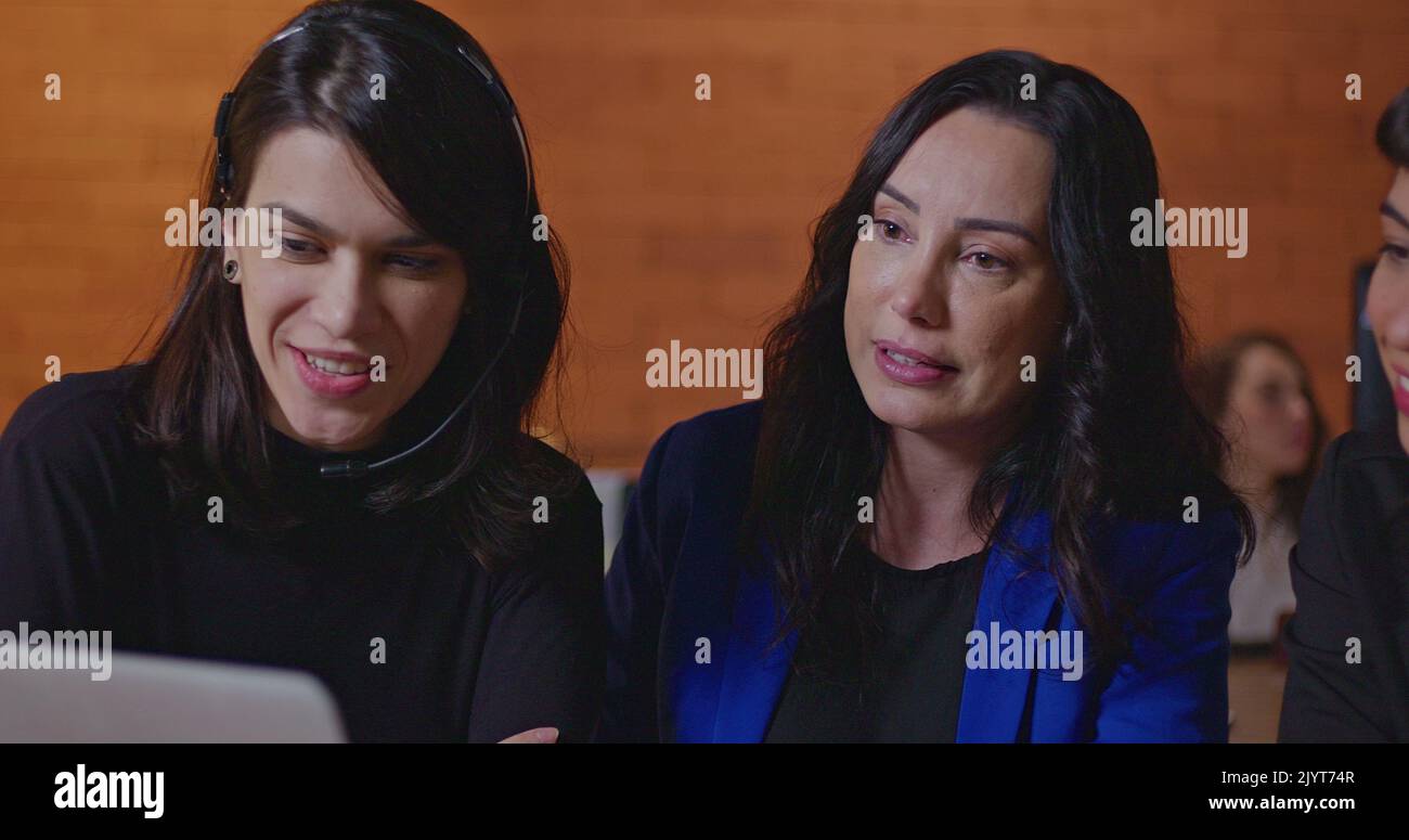 Female executive leader coaching younger staff in front of computers at ...