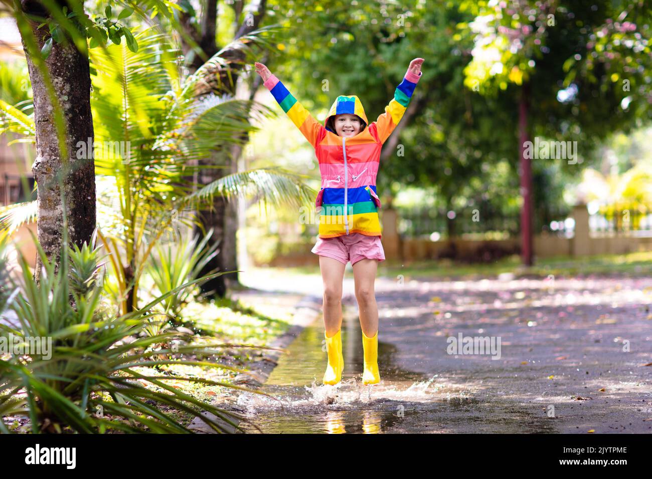 Kid playing in the rain in autumn park. Child jumping in muddy puddle ...