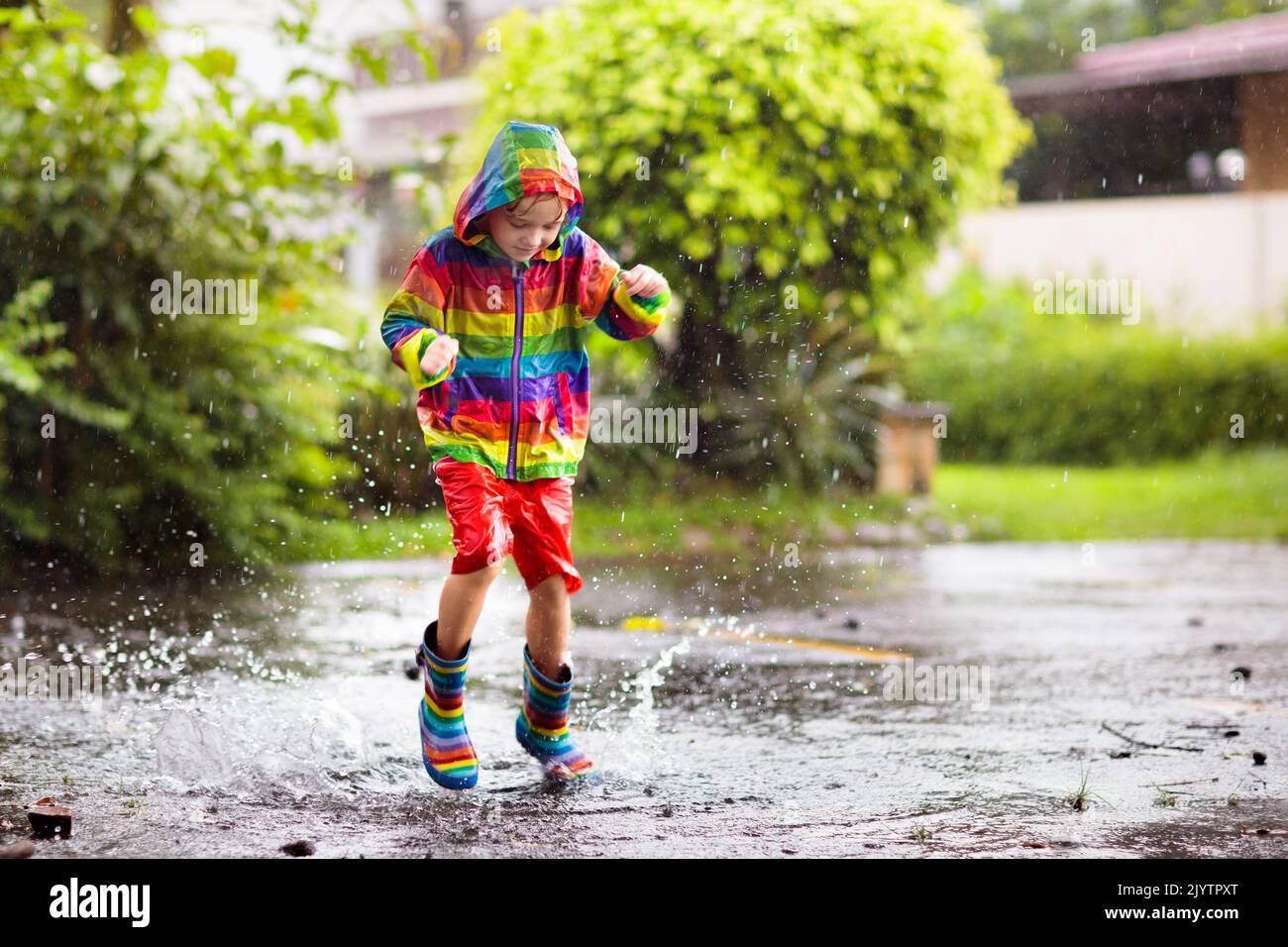 Kid playing in the rain in autumn park. Child jumping in muddy puddle ...