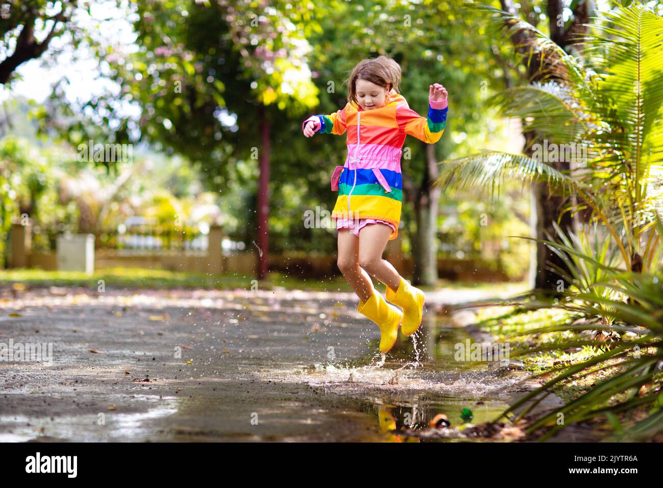 Kid playing in the rain in autumn park. Child jumping in muddy puddle ...