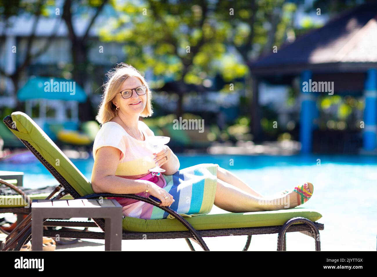 Woman drinking cocktail at swimming pool. Senior lady with exotic drink ...