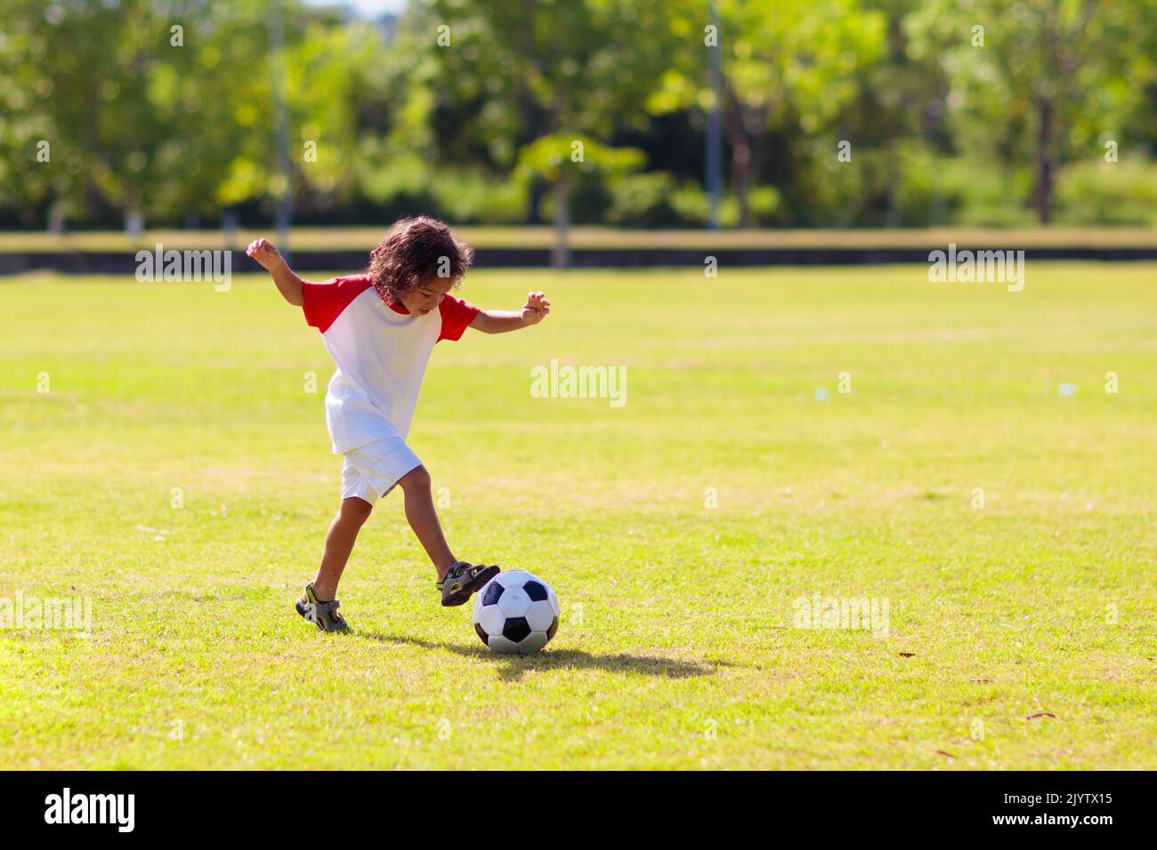 Cute curly little boy playing football. Kids play on outdoor pitch ...