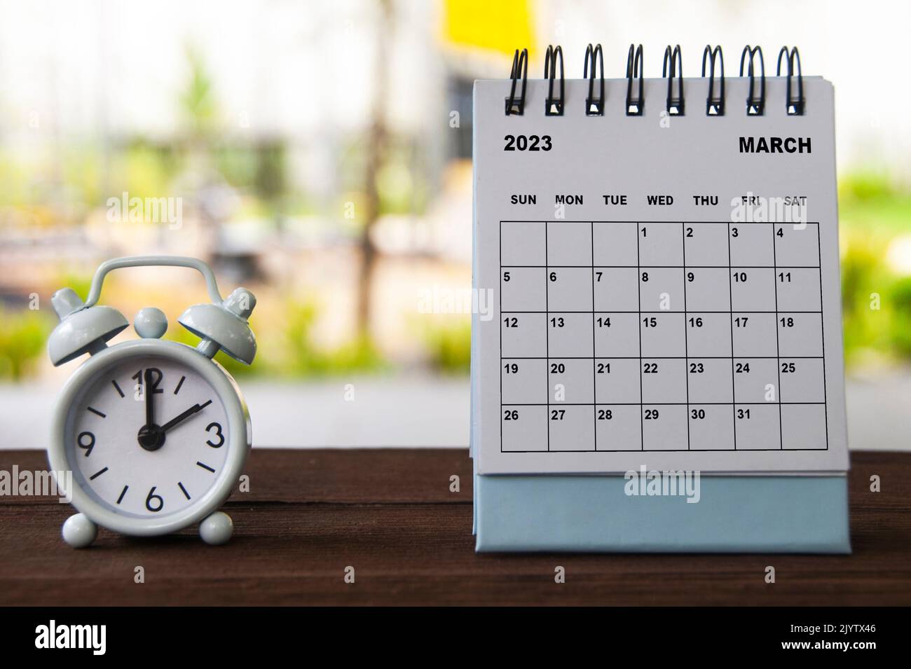 Alarm clock pointing at 2 o'clock with March calendar on a bench. Time ...