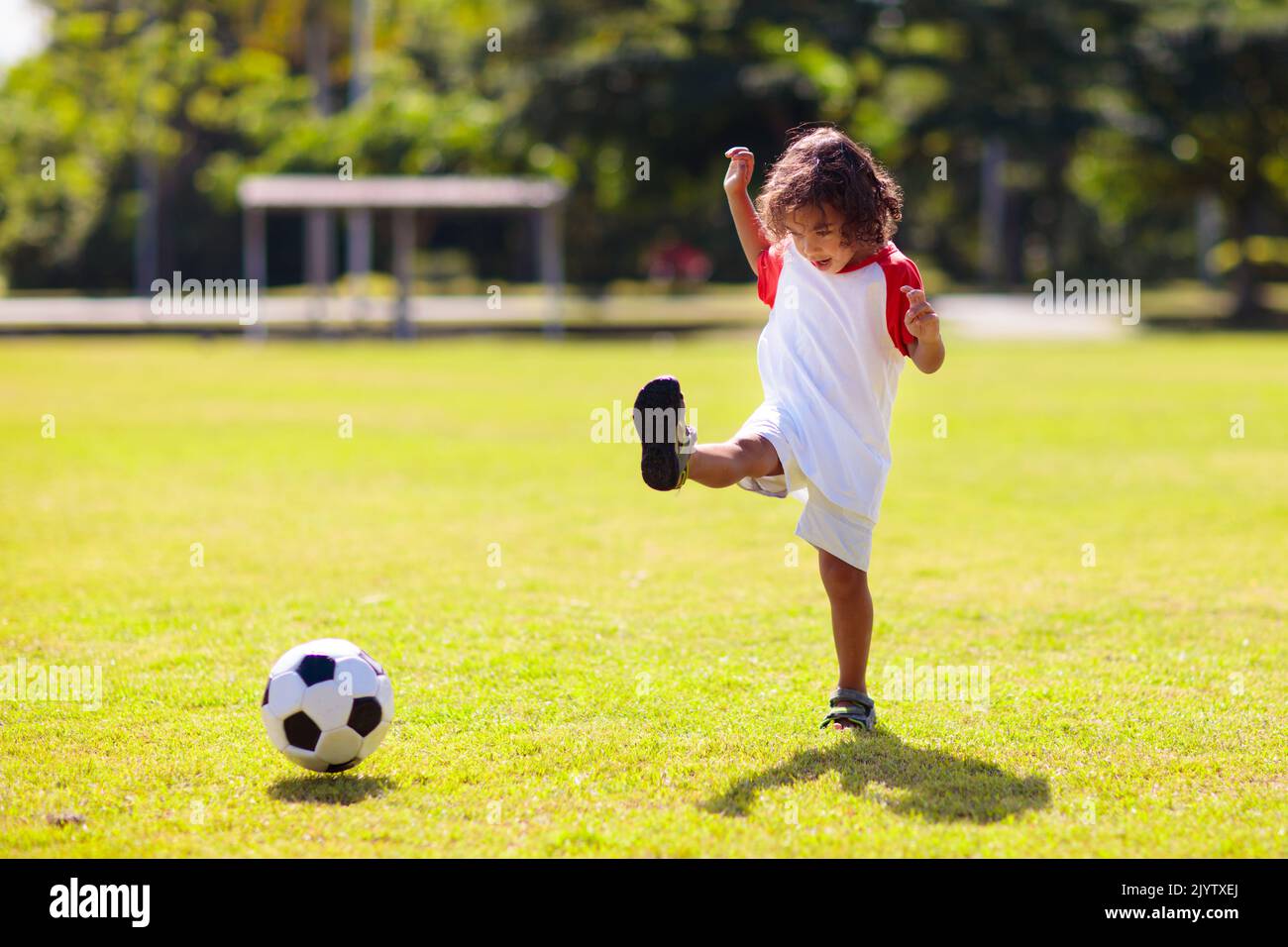 Cute curly little boy playing football. Kids play on outdoor pitch ...