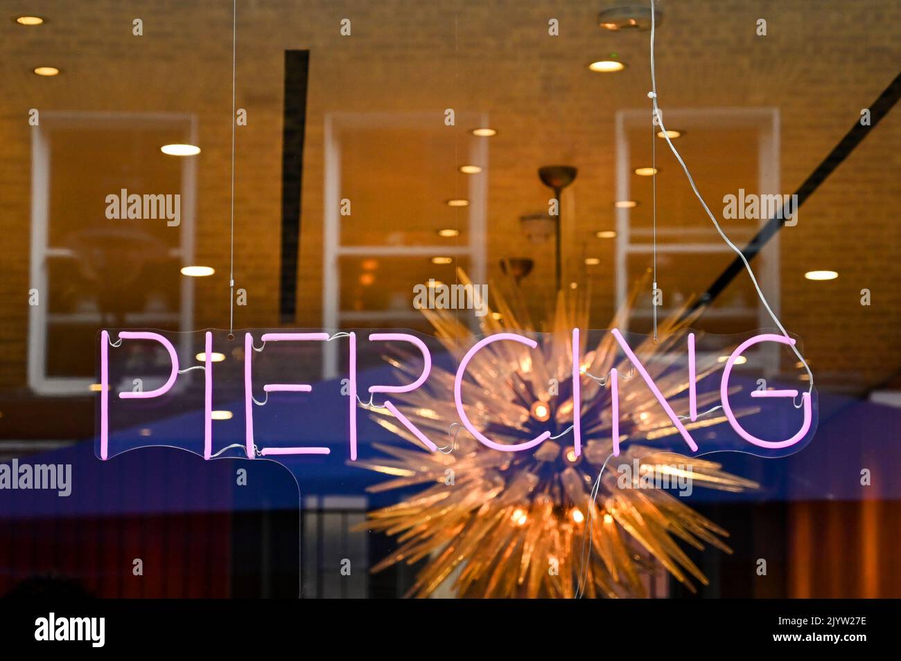 Illuminated sign in the shop window of a body piercing salon. No people ...