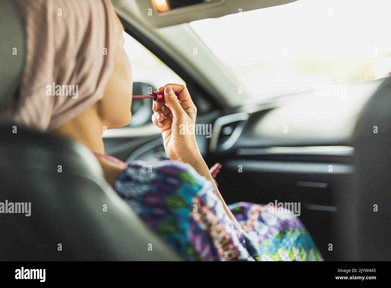 Woman looking in rear view mirror painting her lips doing applying make ...