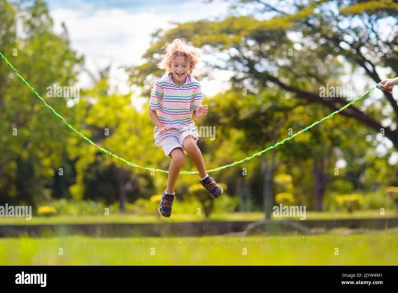 Happy kids play outdoor. Children skipping rope in sunny garden. Summer ...