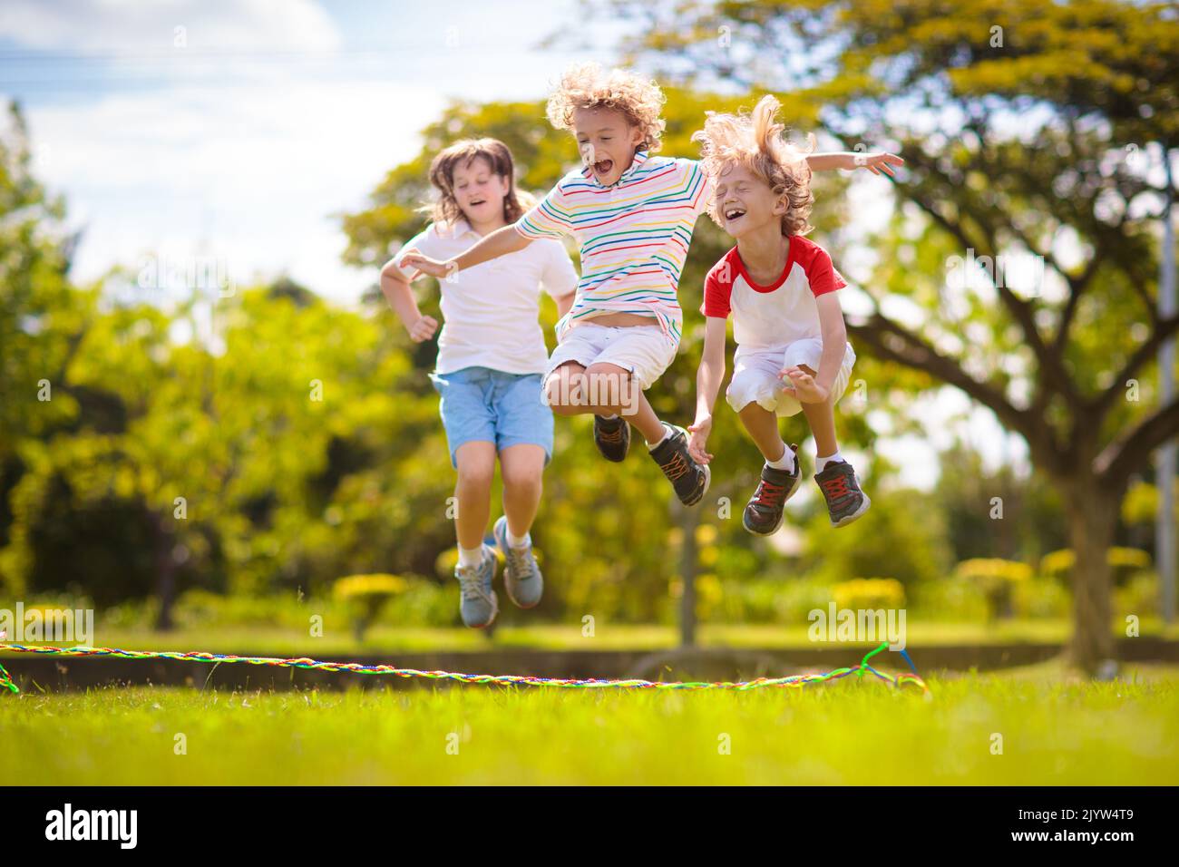 Happy kids play outdoor. Children skipping rope in sunny garden. Summer ...