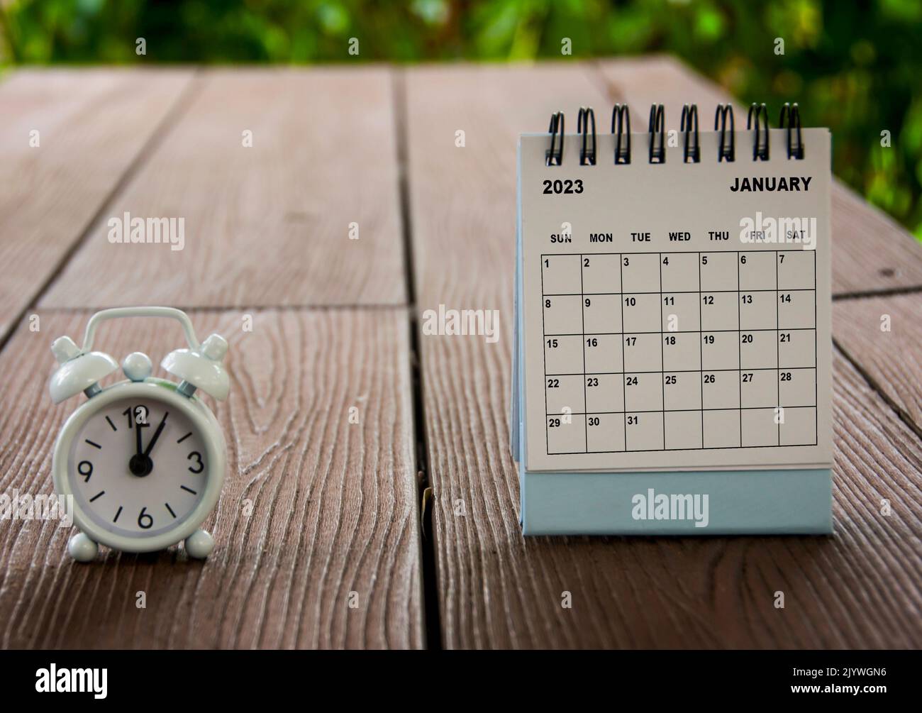 Alarm clock pointing at 1 o'clock with January 2023 calendar on a bench ...
