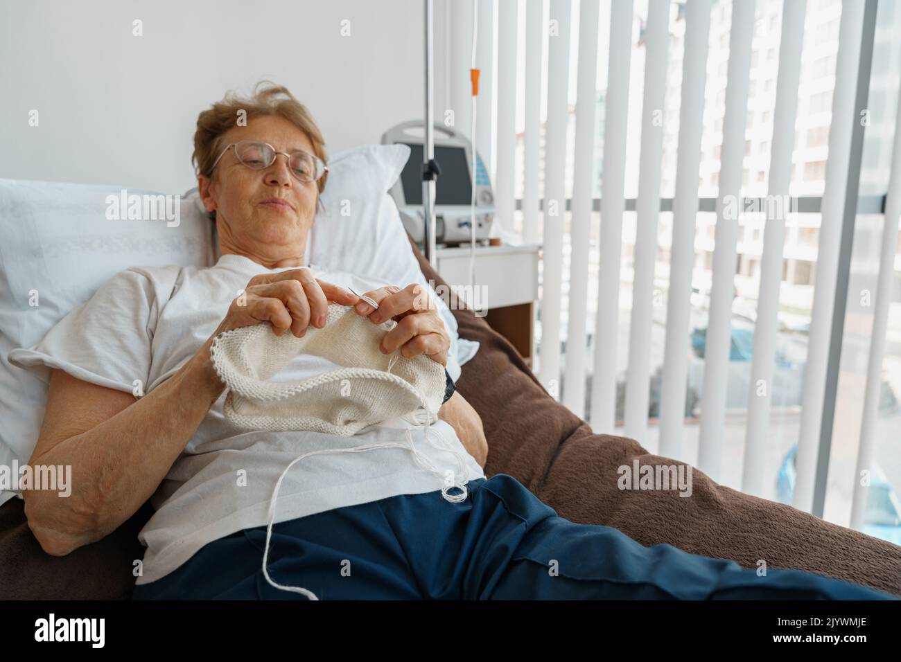Senior patient knits while resting in the hospital ward after medical ...