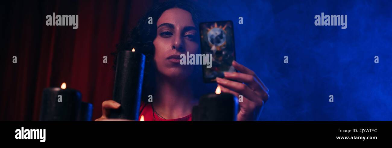 KYIV, UKRAINE - JUNE 29, 2022: young oracle with tarot card and burning ...