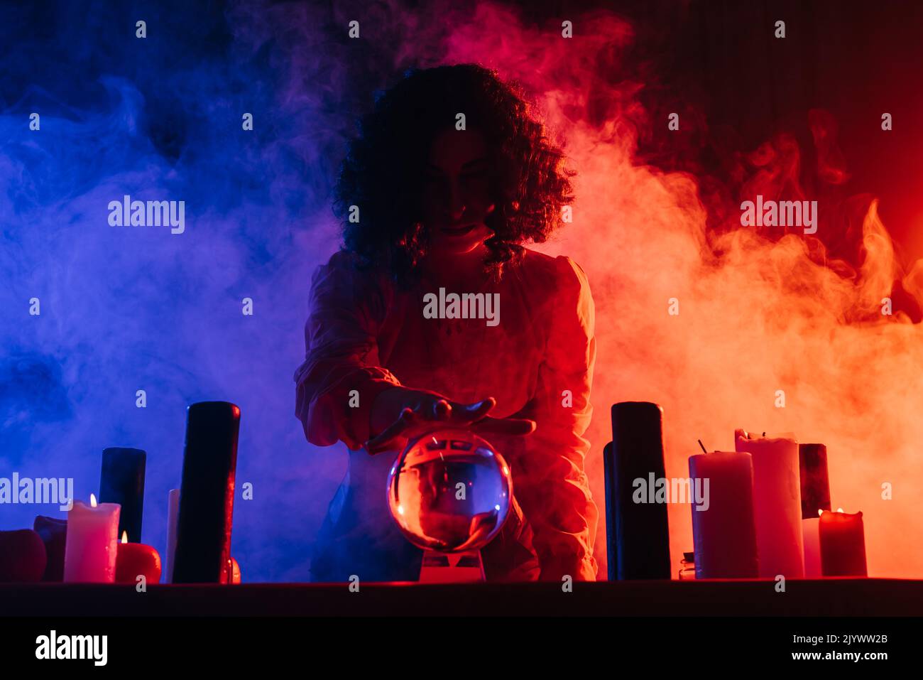 young fortune teller near crystal ball on dark background with colorful ...