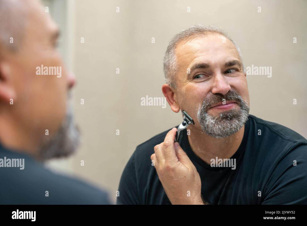 Middle-aged handsome man using razor in bathroom Stock Photo - Alamy