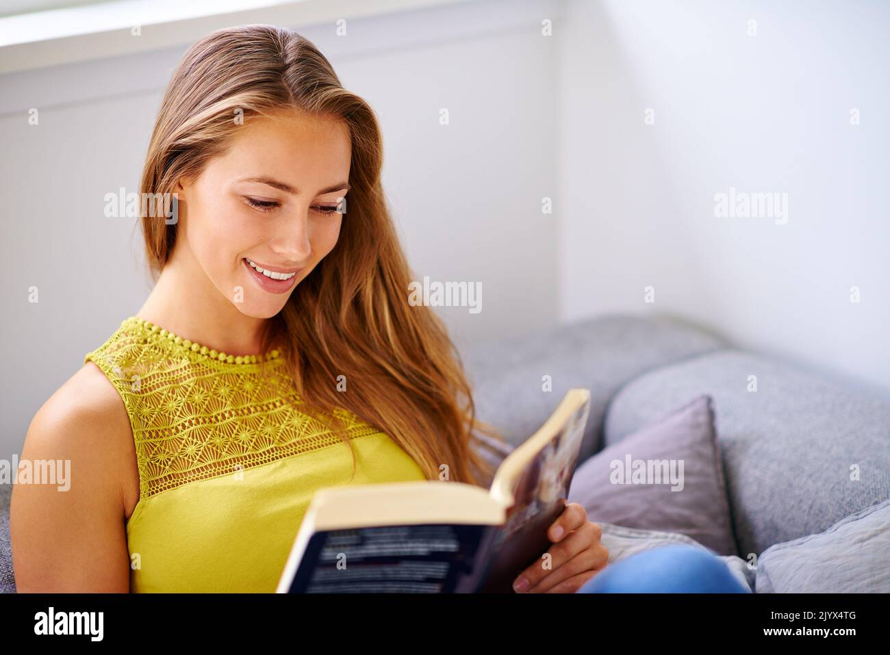 Young woman reading a book with smile on sofa hi-res stock photography ...