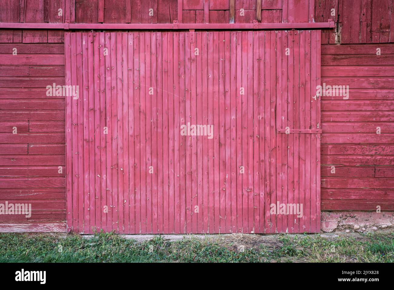 wall of old, wooden, weathered red painted barn with a sliding gate ...