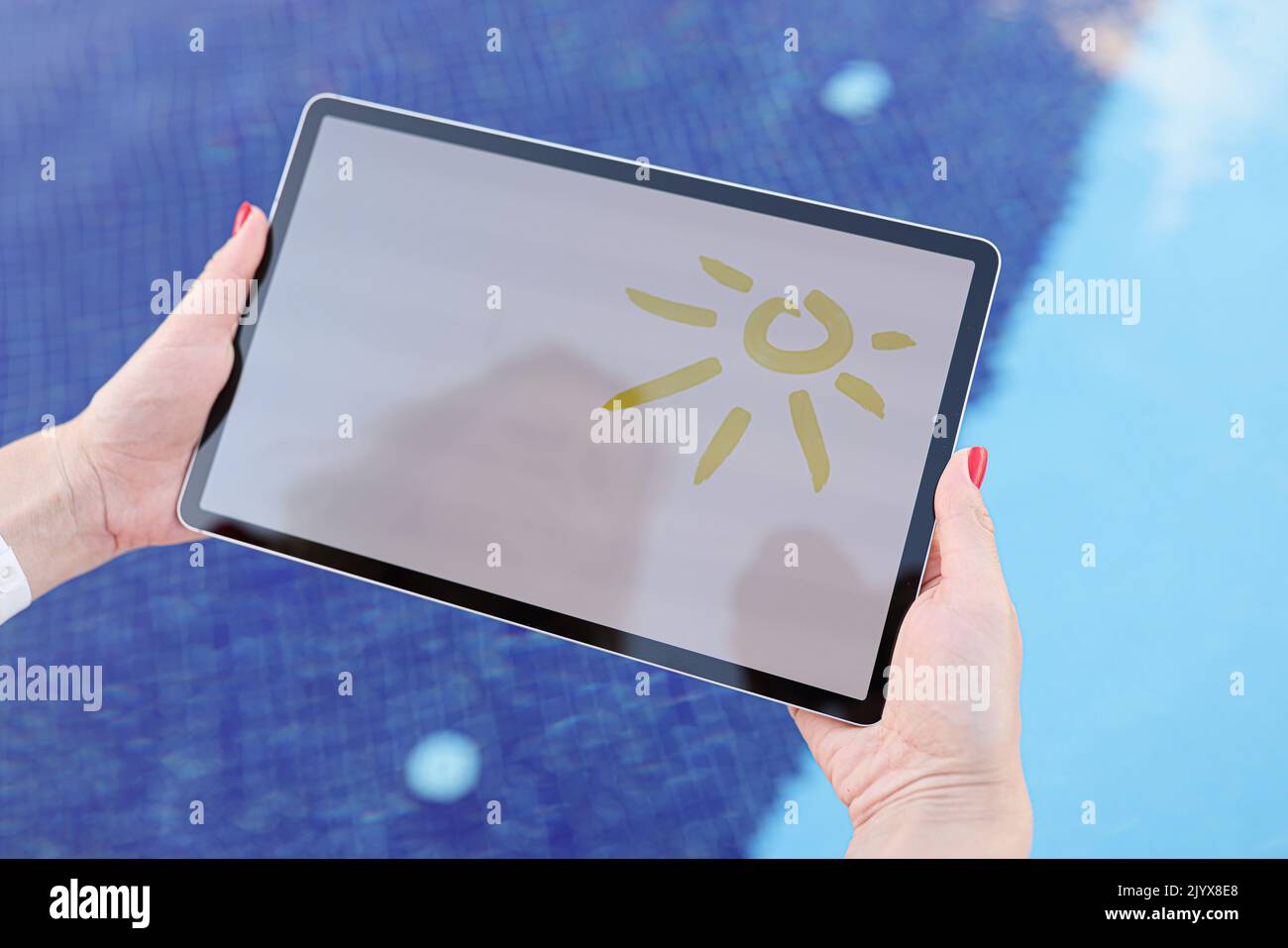 Female hands hold tablet with drawn sun and white screen above pool ...