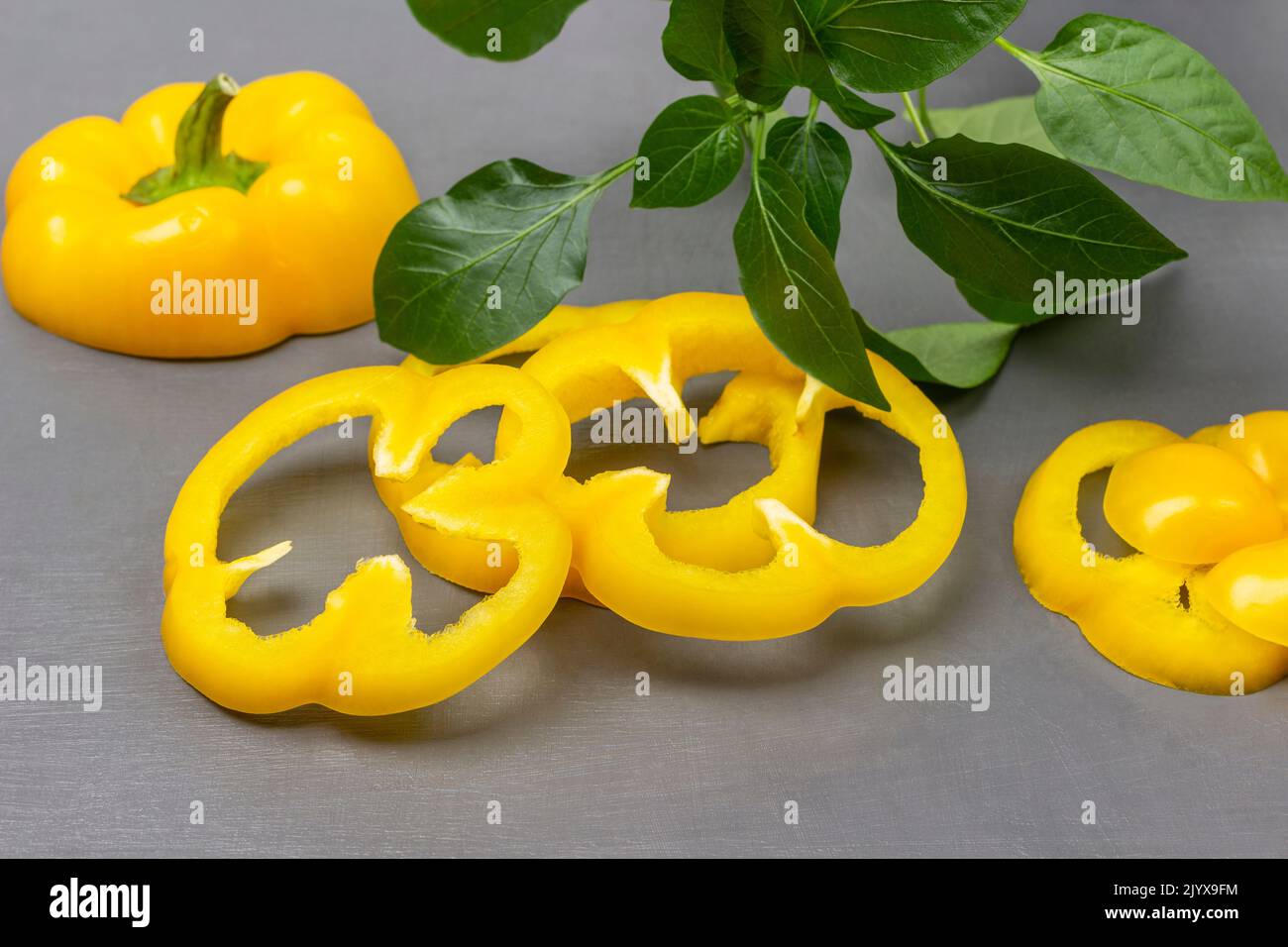 Sliced yellow pepper and green leaves of pepper plant. Top view. Grey ...
