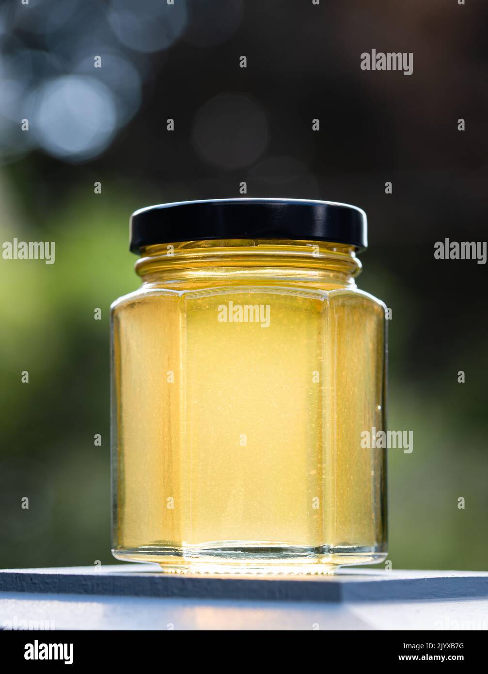 Small jar of honey outside against a green background Stock Photo - Alamy