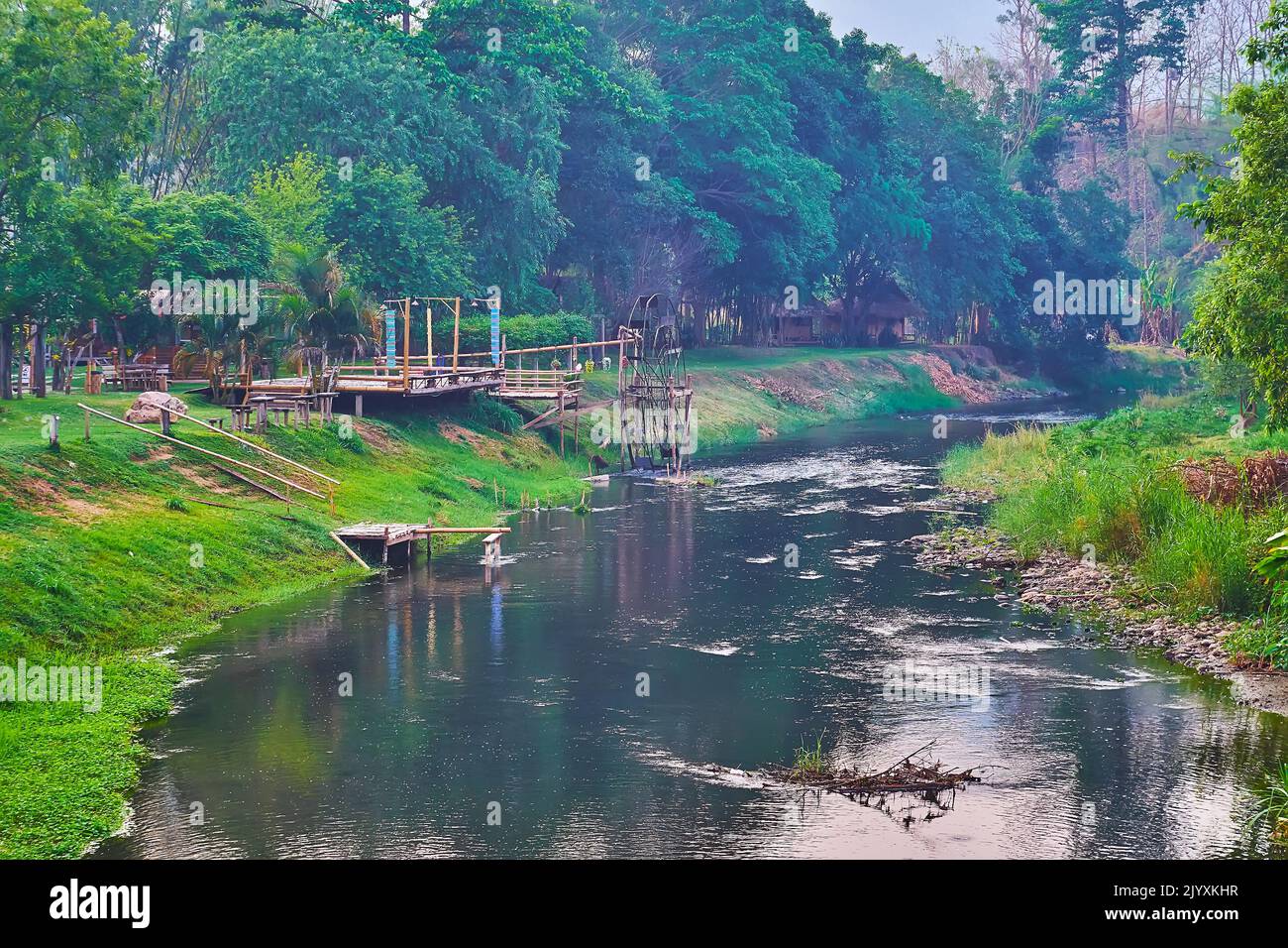 The foggy sunrise on Pai river with old water wheel and lush green ...