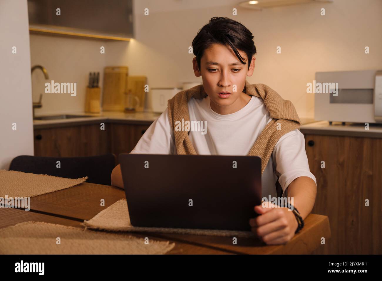 Asian boy working with laptop while sitting in kitchen at home Stock ...