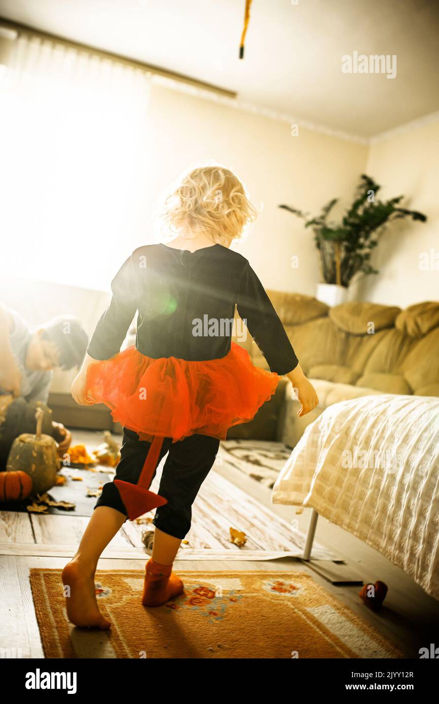 A girl in a Halloween devil costume walks through a room lit up by the ...