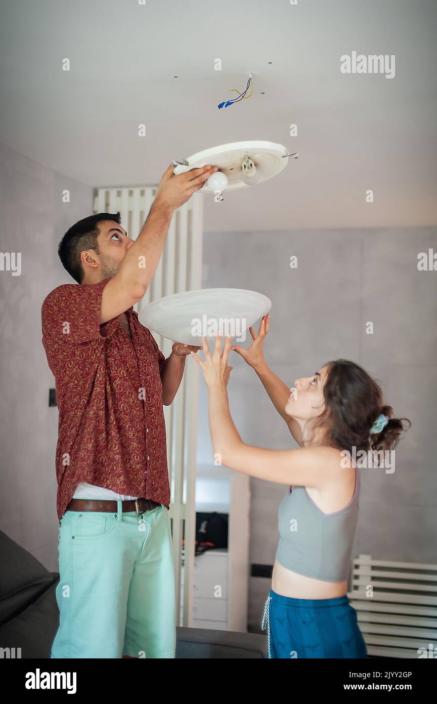 Living together, young man and woman install a ceiling light ...