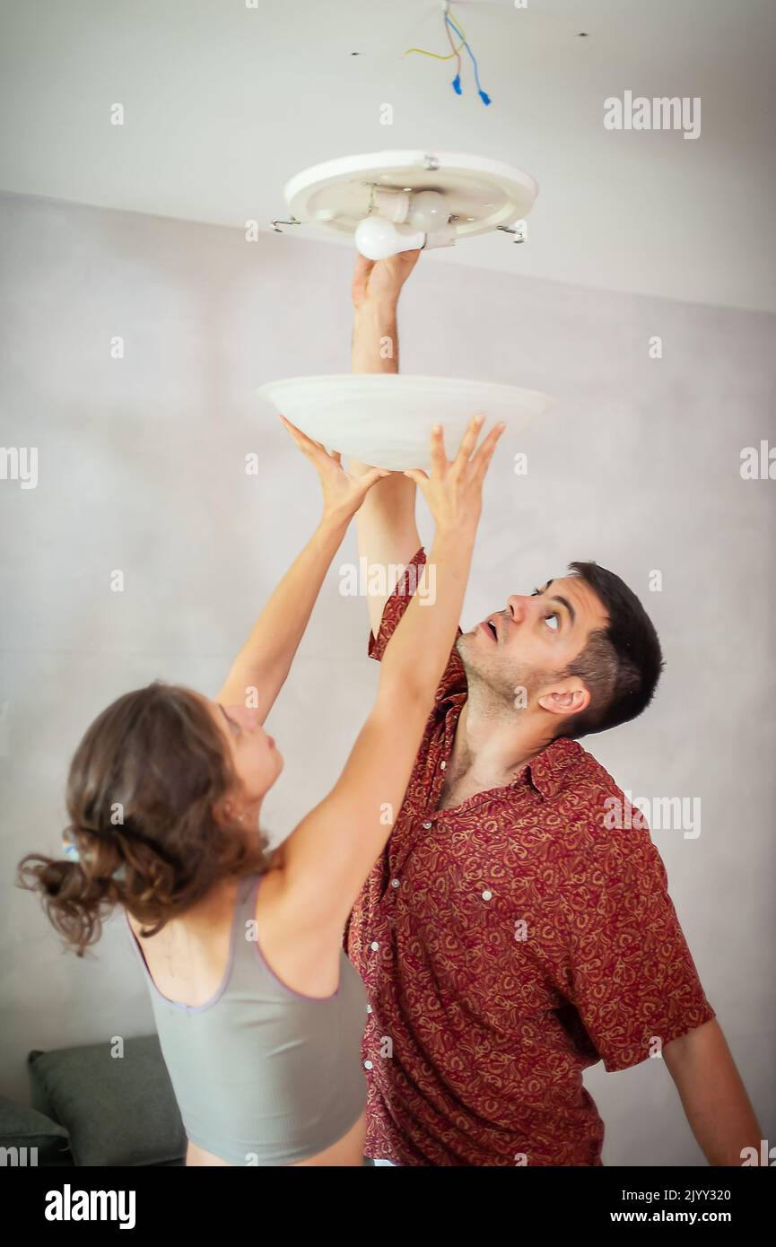 Living together, young man and woman install a ceiling light ...