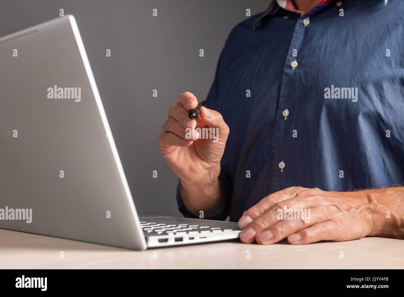 E-signature. Man sitting at table with laptop and holding pen for signing electronic document ...