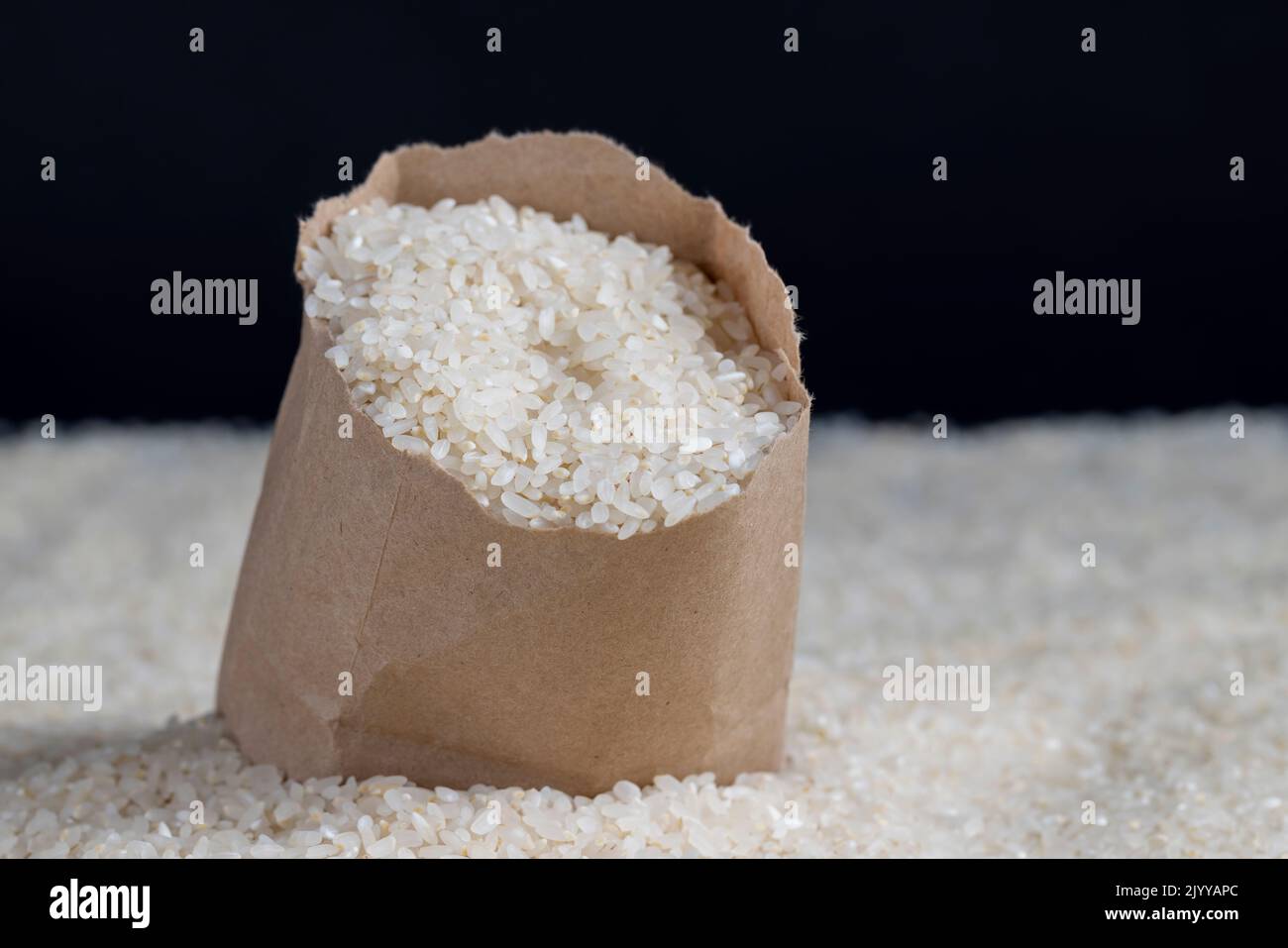 a pile of white rice in a paper bag and on the table, white uncooked ...