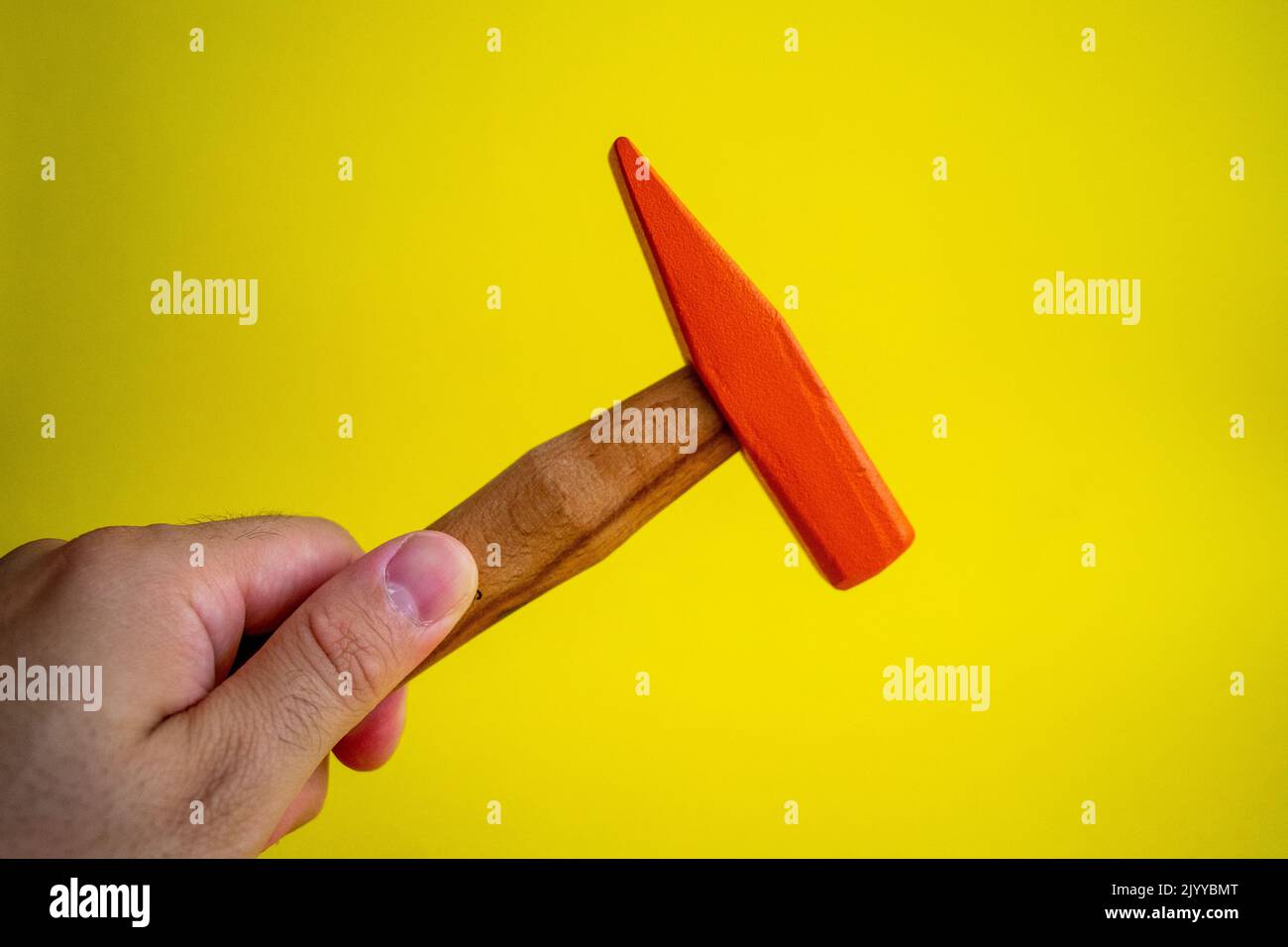 Hand held wooden handle hammer and orange head, isolated yellow ...