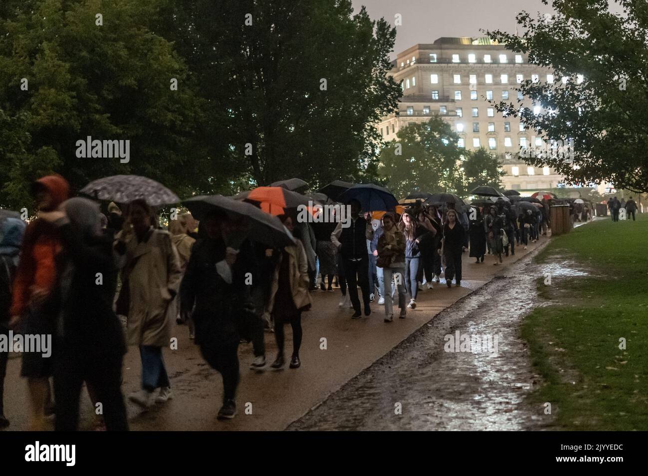 Members of the public walk in the rain through green park towards ...