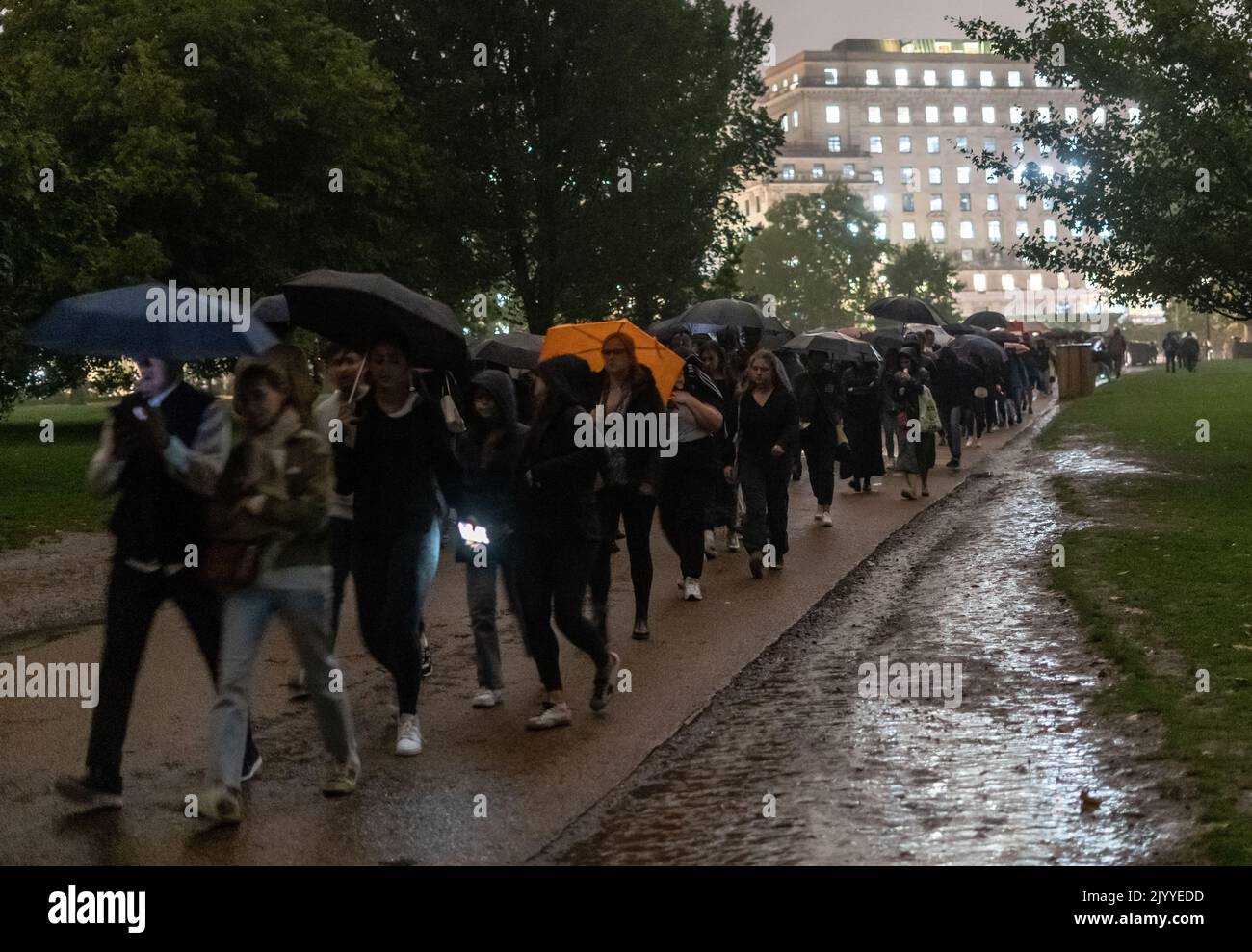 Members of the public walk in the rain through green park towards ...