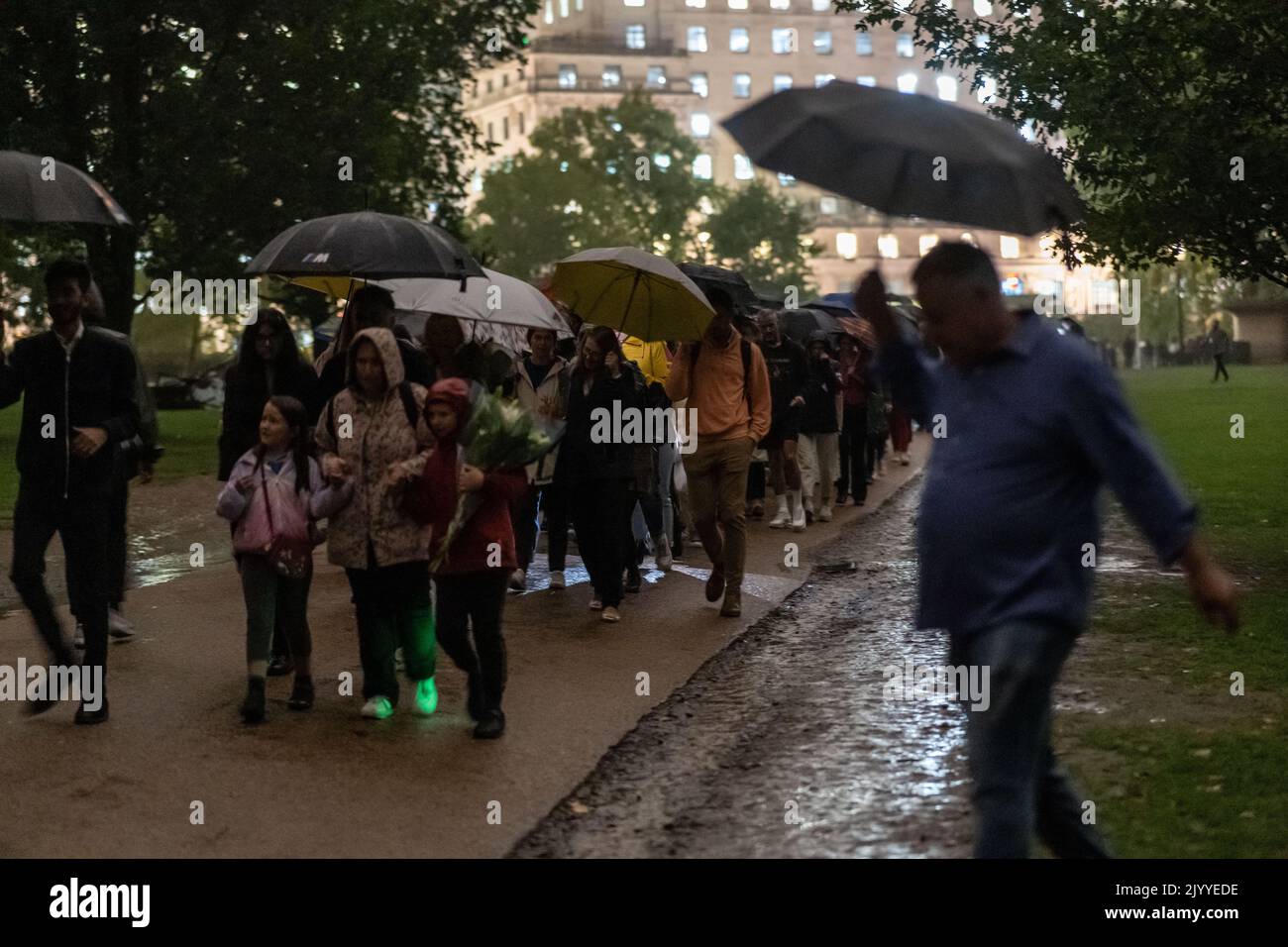 Members of the public walk in the rain through green park towards ...