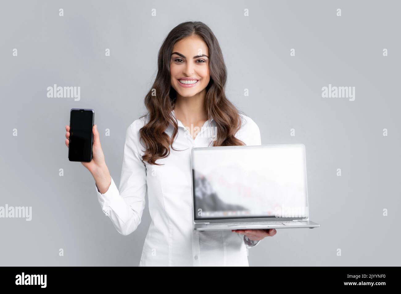 Smiling girl using mobile phone and laptop. Woman showing empty laptop screen, mock up template ...