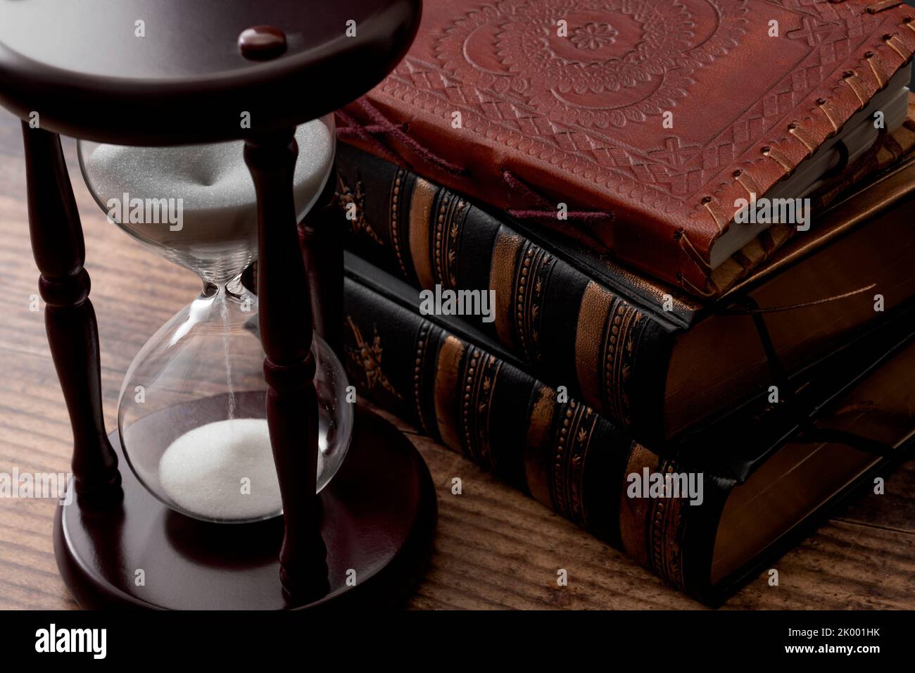 Sand flowing in vintage hourglass next to stack of ragged books concept ...