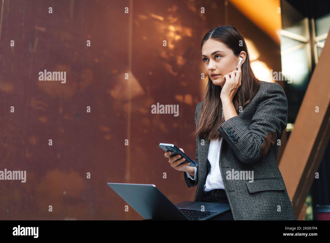 Young professional business woman wearing suit using wireless earphones ...