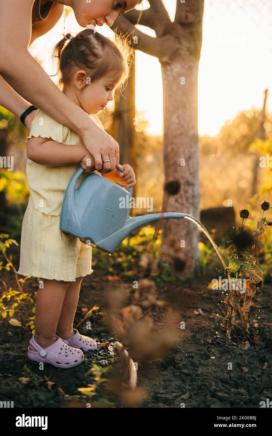 Mother helping her little baby girl watering flowers with watering ...