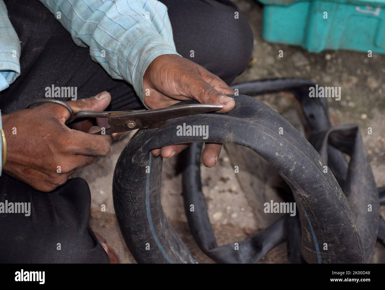 Hand of a cycle mechanic cutting a part of a tyre tube which he will ...