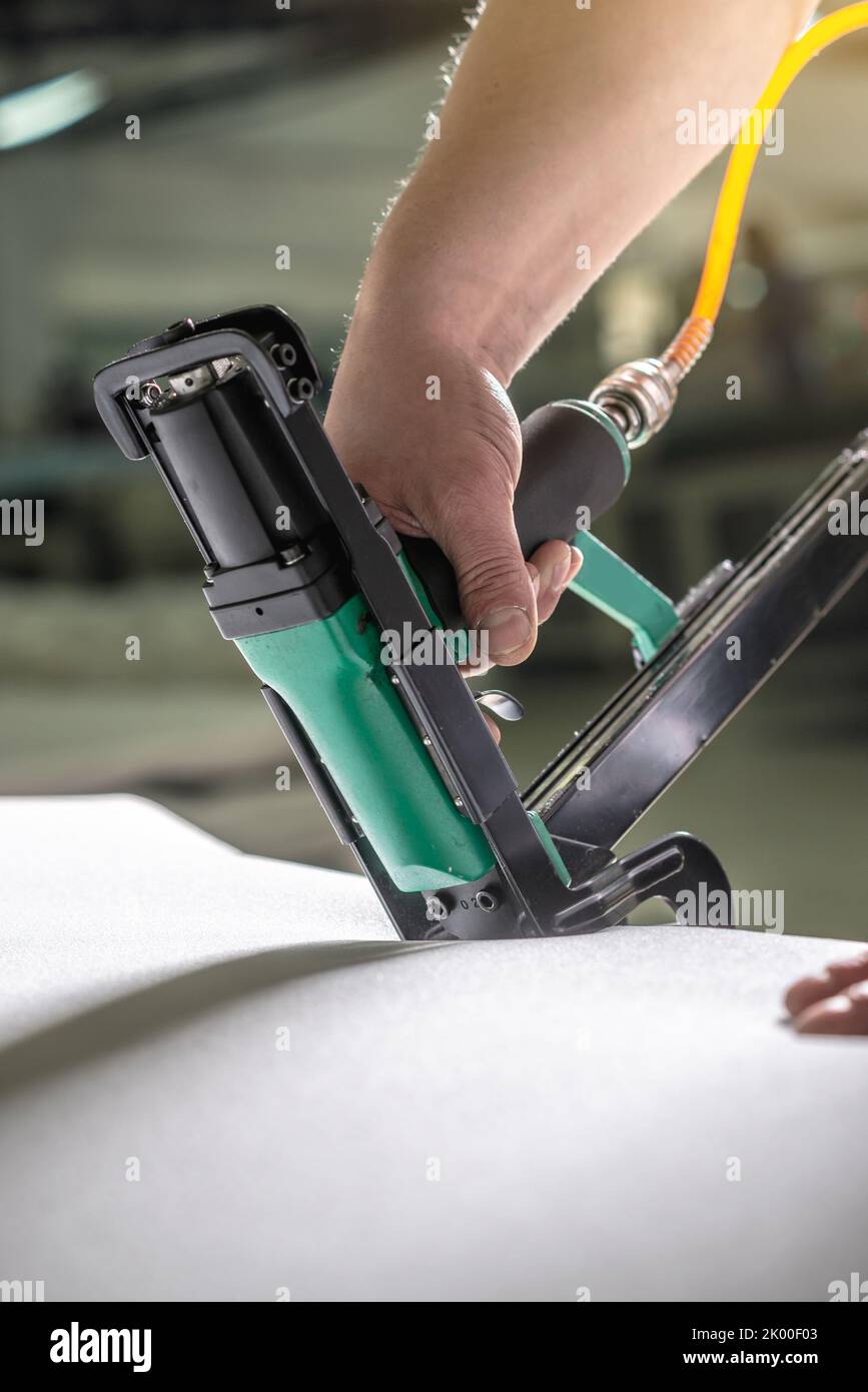 An employee holds in his hands an industrial air stapler for sheathe ...