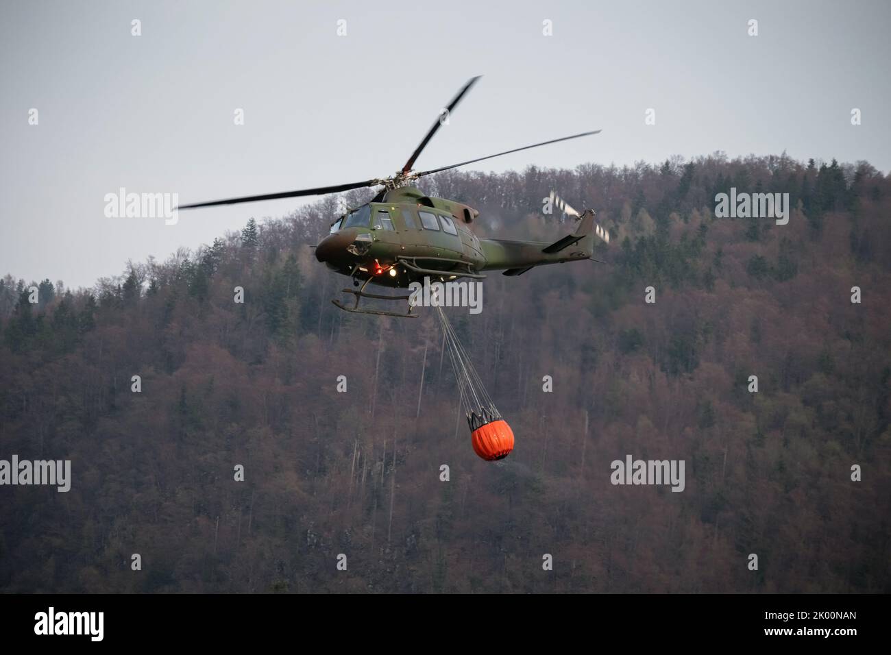 Firefighting helicopter with a bucket suspended on a cable, collecting ...