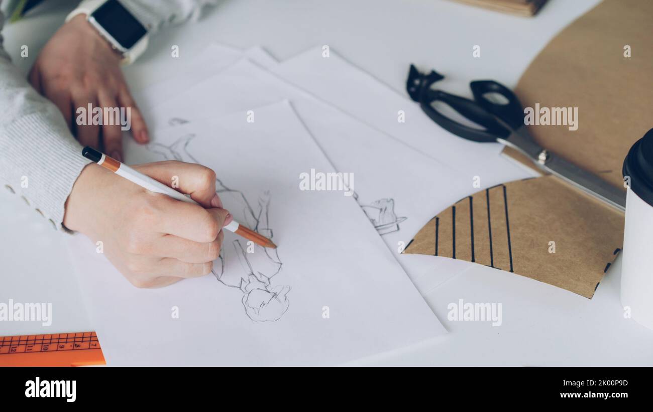 Close-up of fashion designer is drawing lines on clothing sketch. Woman ...