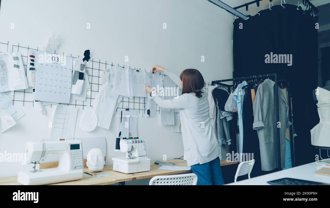 Female clothing designer is taking sketches from studio table and ...