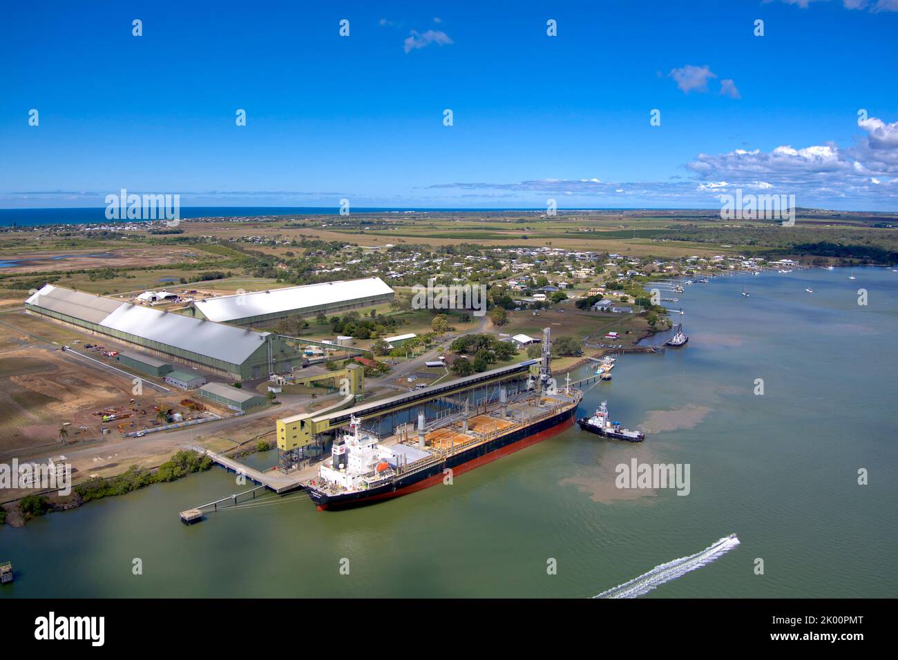 Aerial view of a cargo ship being loaded at a terminal by the coastline ...