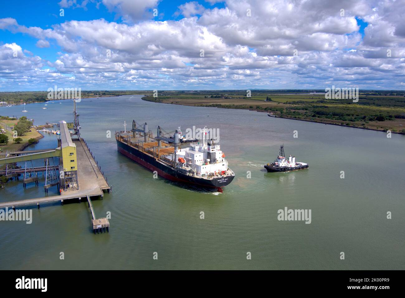 Aerial view of cargo ship being guided by a tugboat at a commercial ...