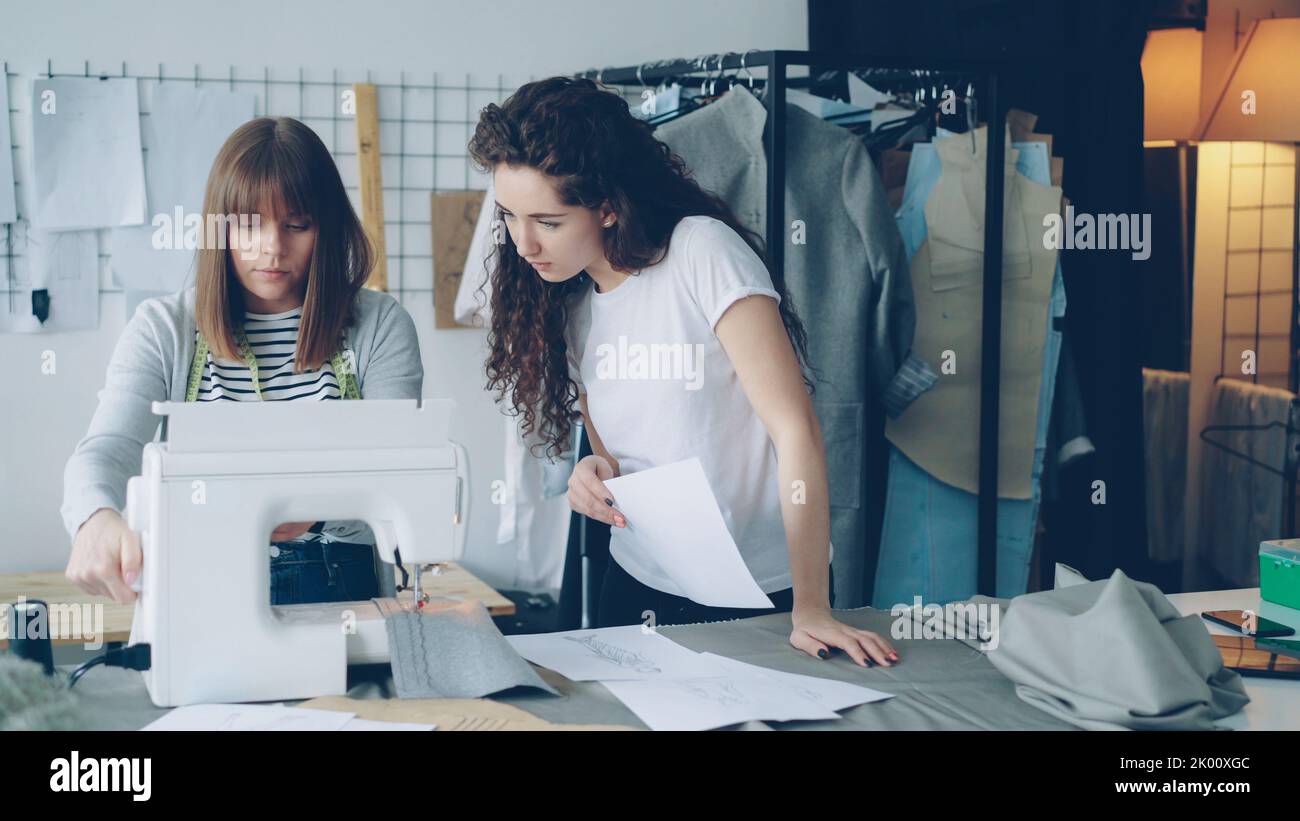Attractive female dressmakers are looking at sketches and working with ...