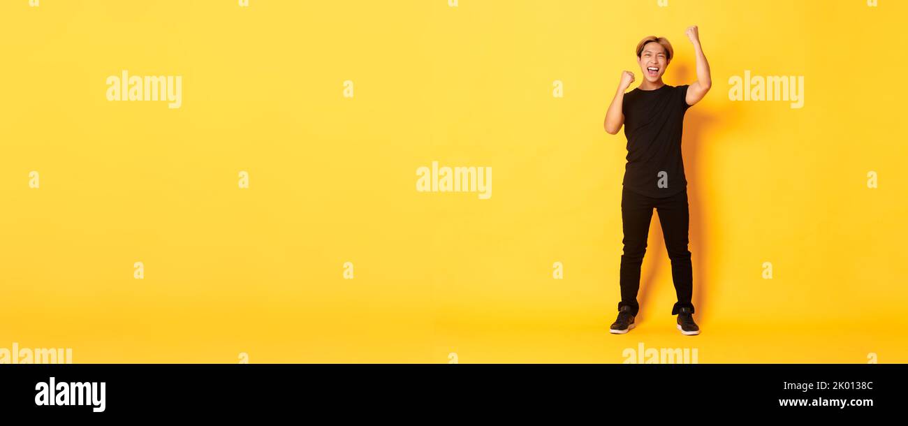Full-length of triumphing handsome asian man with blond hair, raising ...