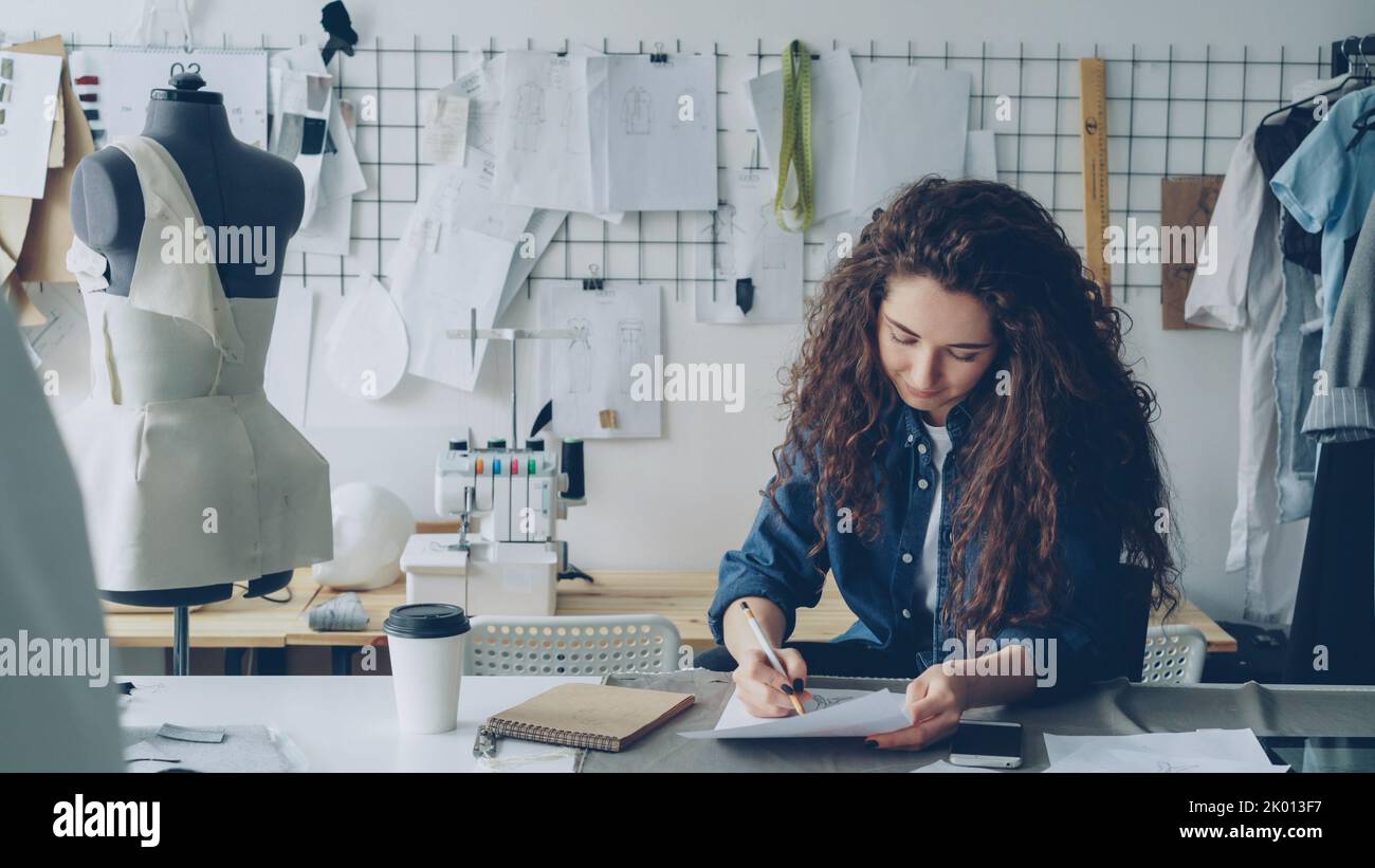 Young woman fashion designer is drawing ladies' garment sketch at desk ...