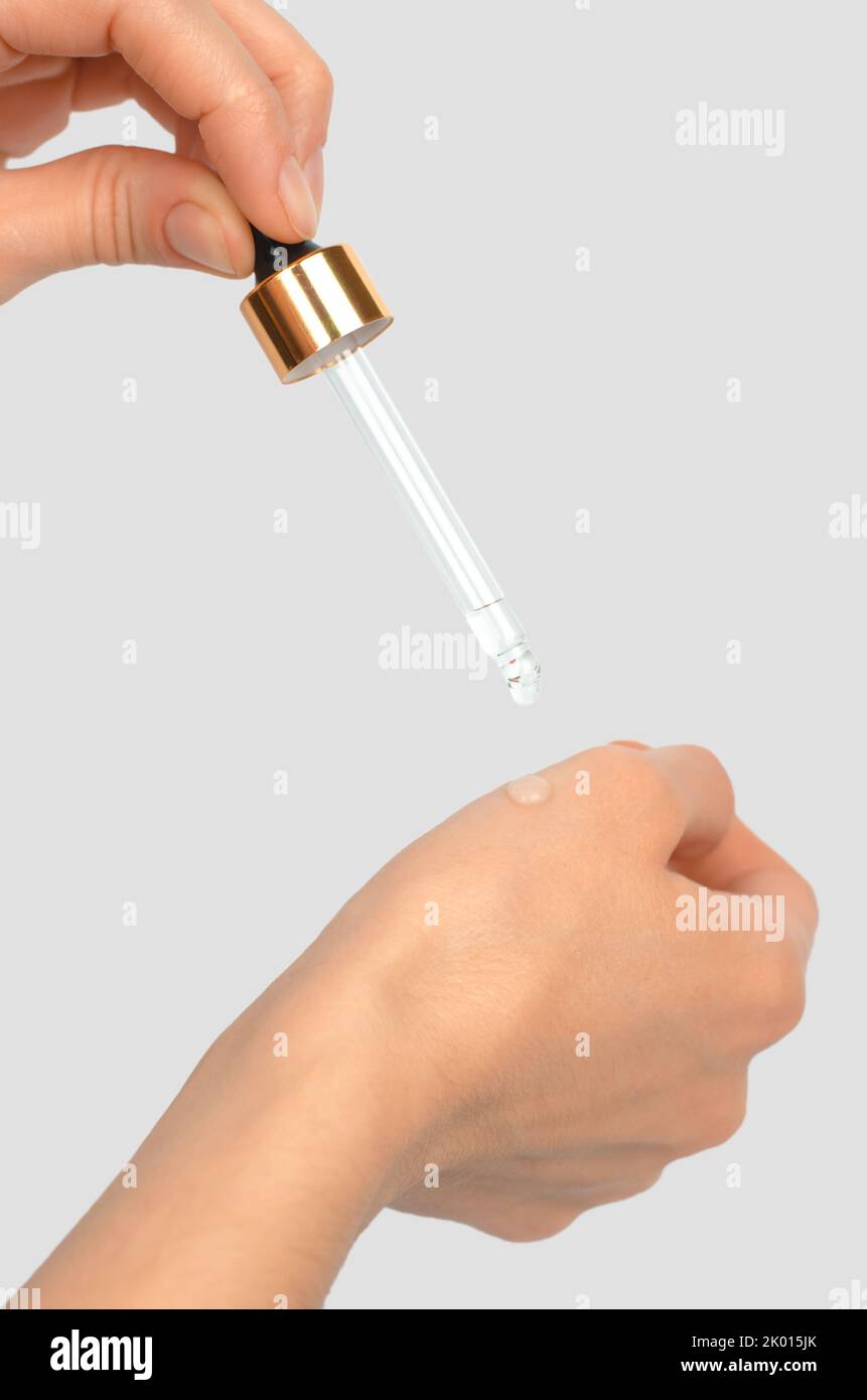 A glass pipette in a woman's hand drips essential oil onto her hand ...